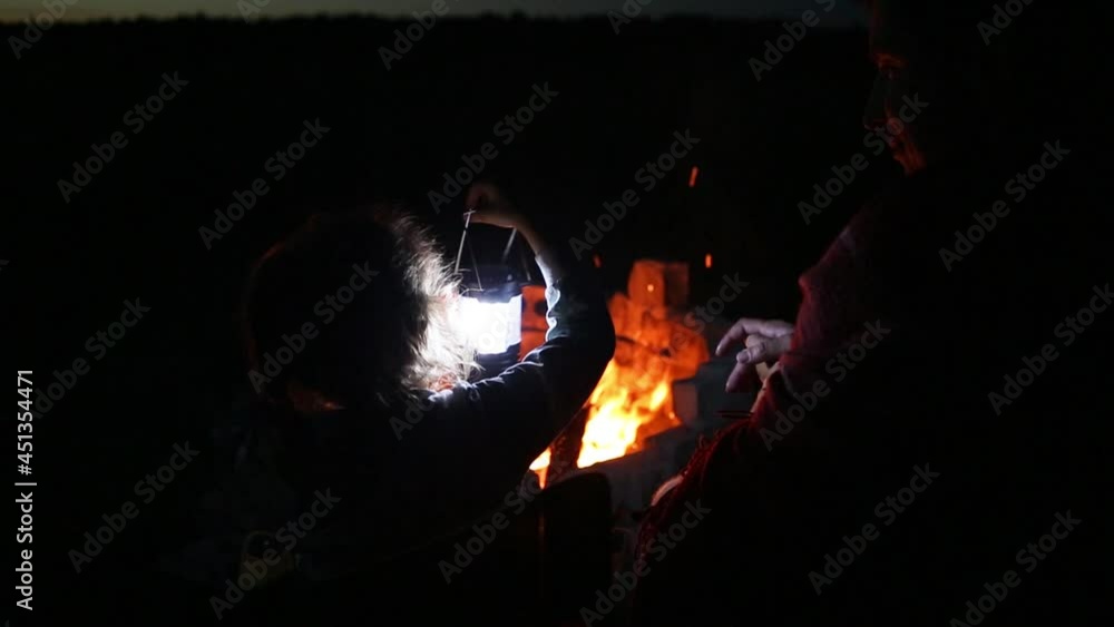 Dad and daughter sit at night by the fire in the open air in the summer ...