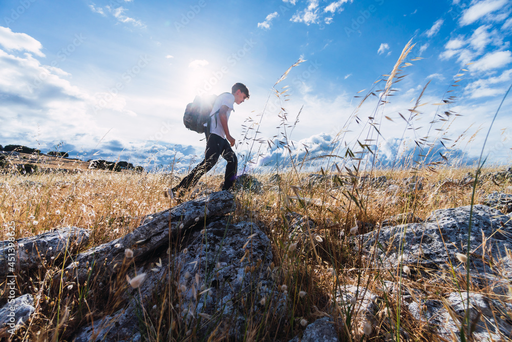 Side view of a teenager carrying backpack hiking through rocky valleys ...