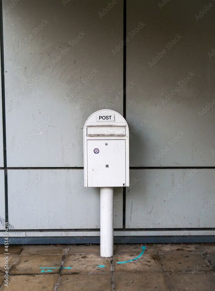 Small, white post box outside in front of a dirty white wall with black ...