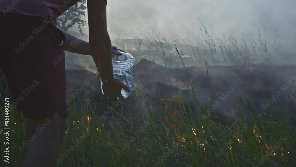 Vídeo do Stock: A volunteer man or boy extinguishes a wild fire. Pours ...