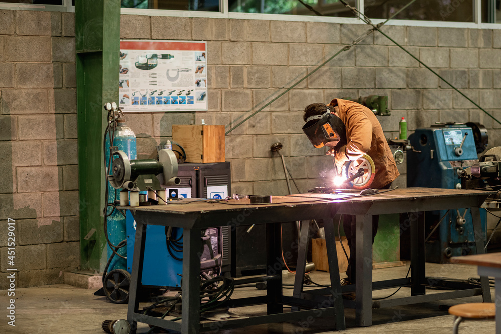 Hombre soldando en un taller con protección para el rostro y sus cuerpo ...