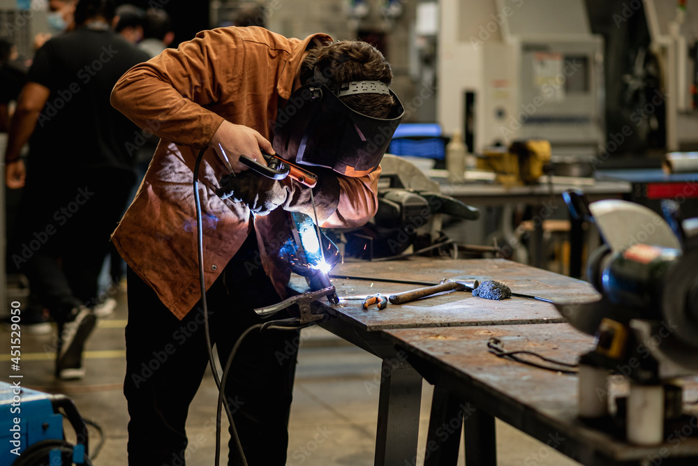 Hombre soldando en un taller con protección para el rostro y sus cuerpo ...