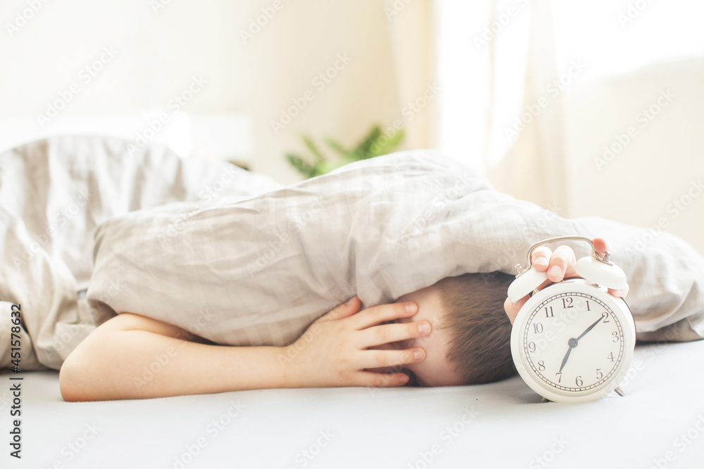 boy lying on the bed and stopping alarm clock in morning. childs hand ...
