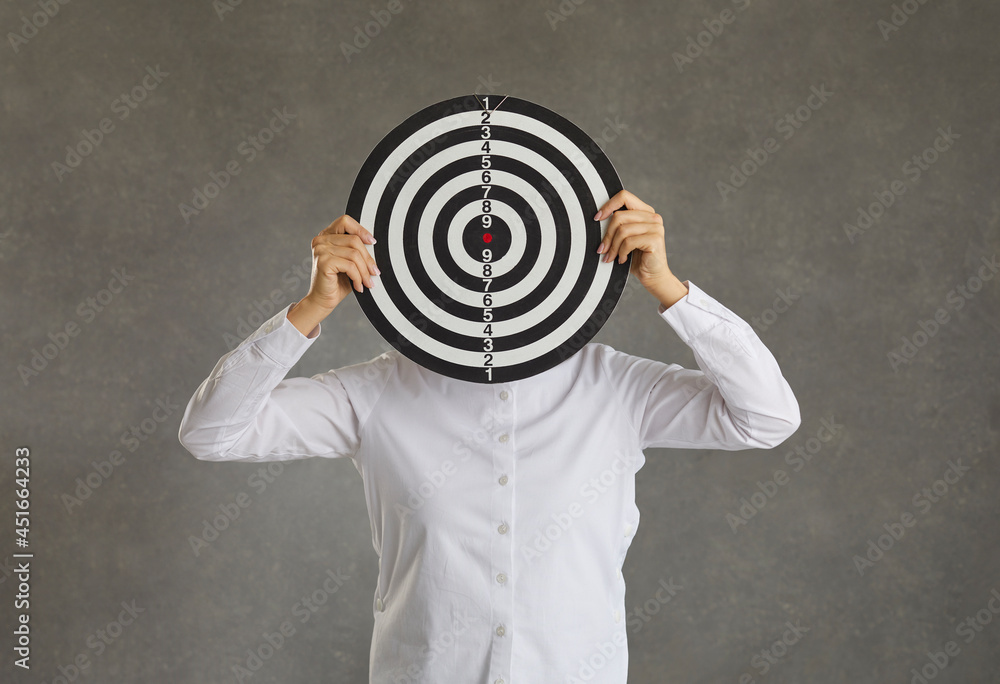 Woman hiding her face behind a shooting target standing on a grey ...