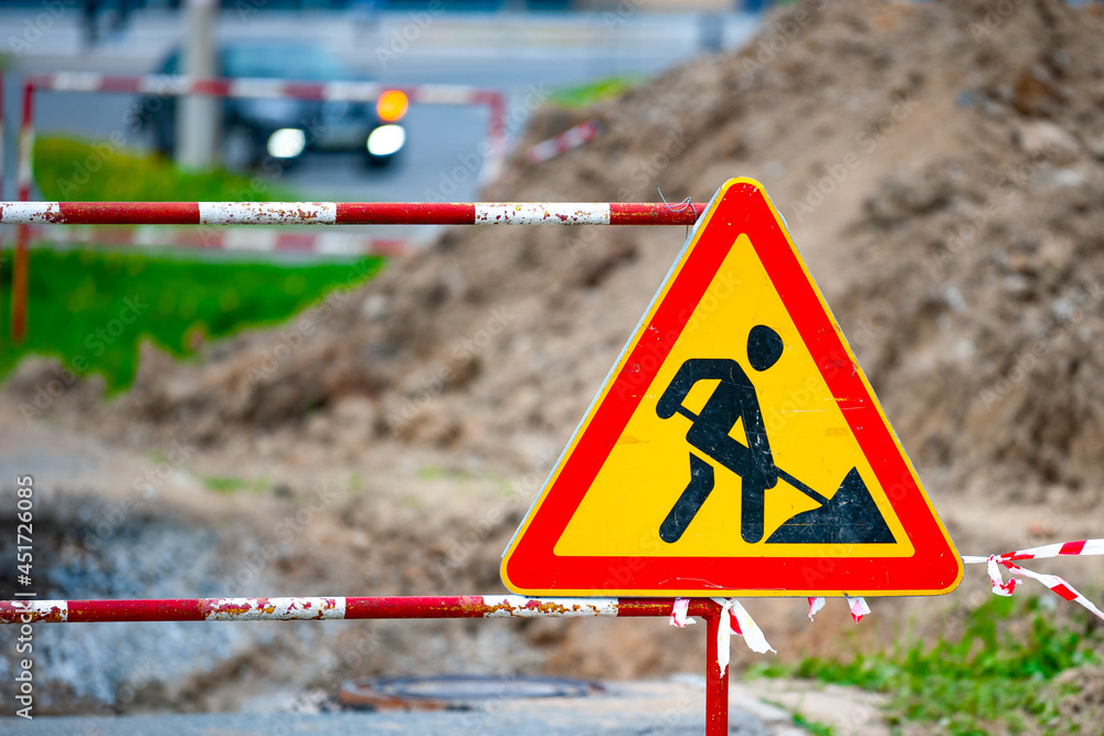 Warning road sign. Road construction work is underway behind a metal ...