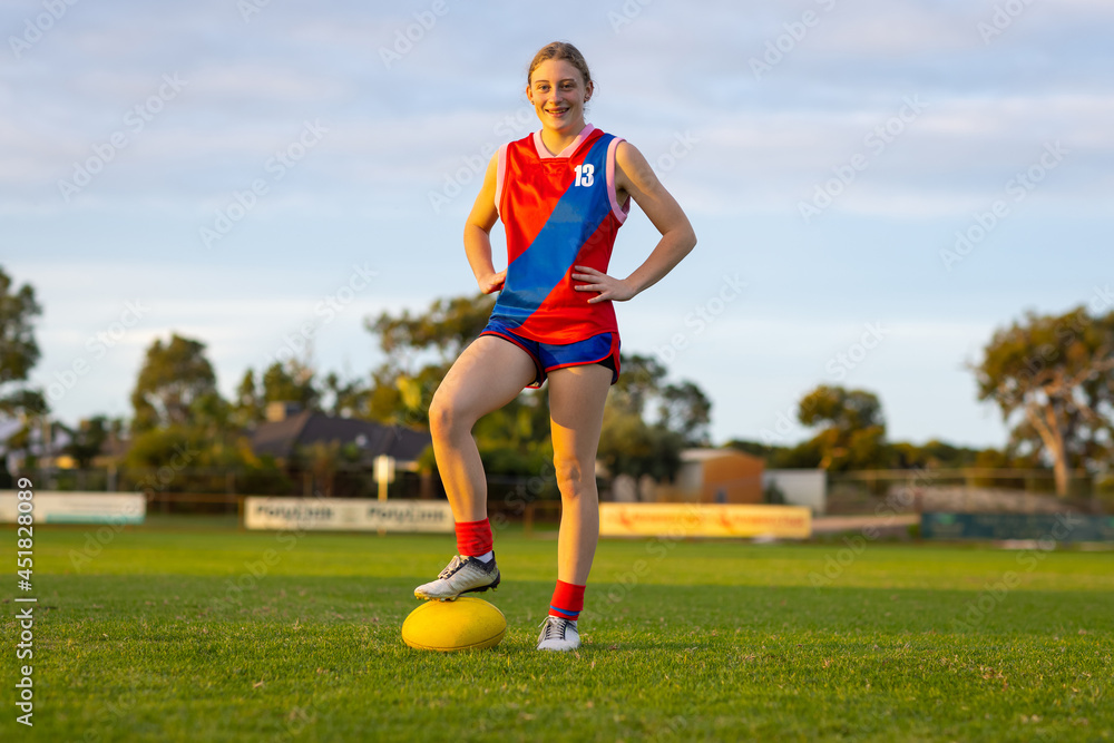teenage girl in uniform standing on football oval with foot on ball ...