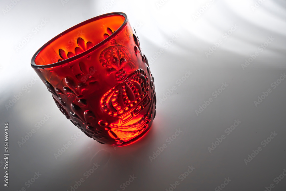 A vessel, a wide glass of red glass with a volumetric pattern along the ...