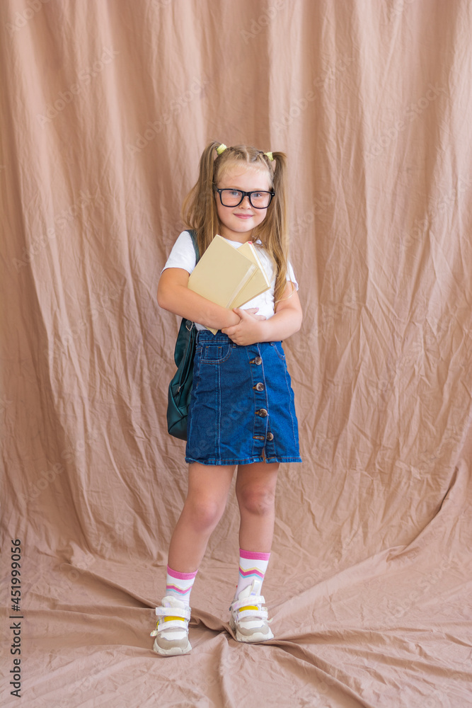 Cheerful little girl schoolgirl back to school hugging book on studio ...