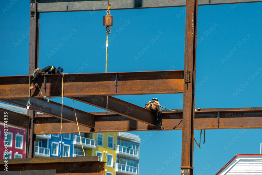 A male steelworker or construction worker sits on a steel beam of a ...