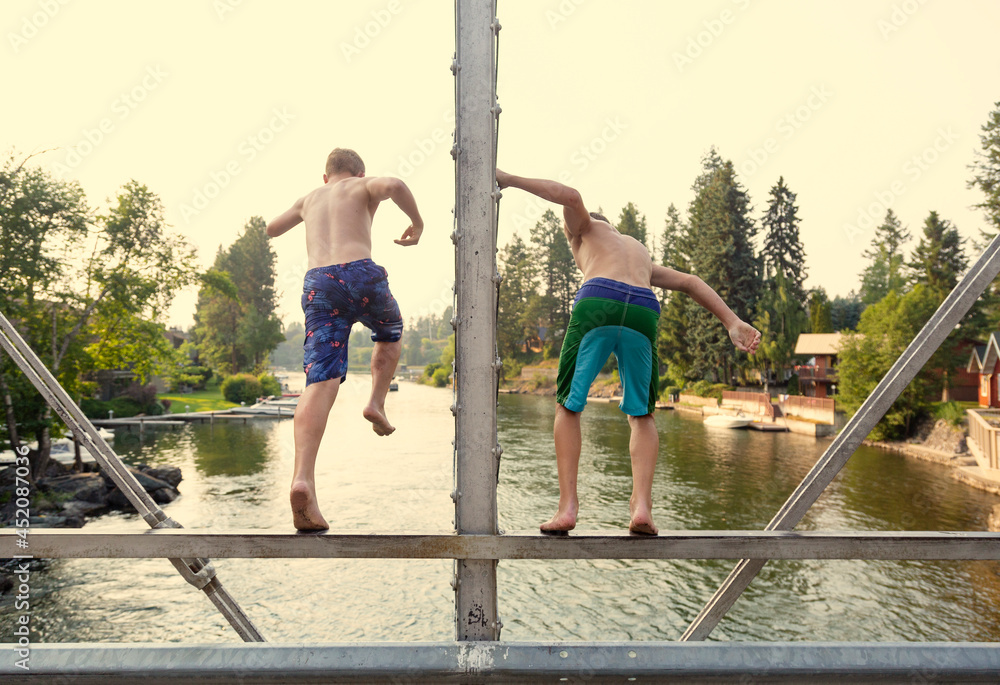 Daring young boys jumping off a bridge into the river. View from behind ...