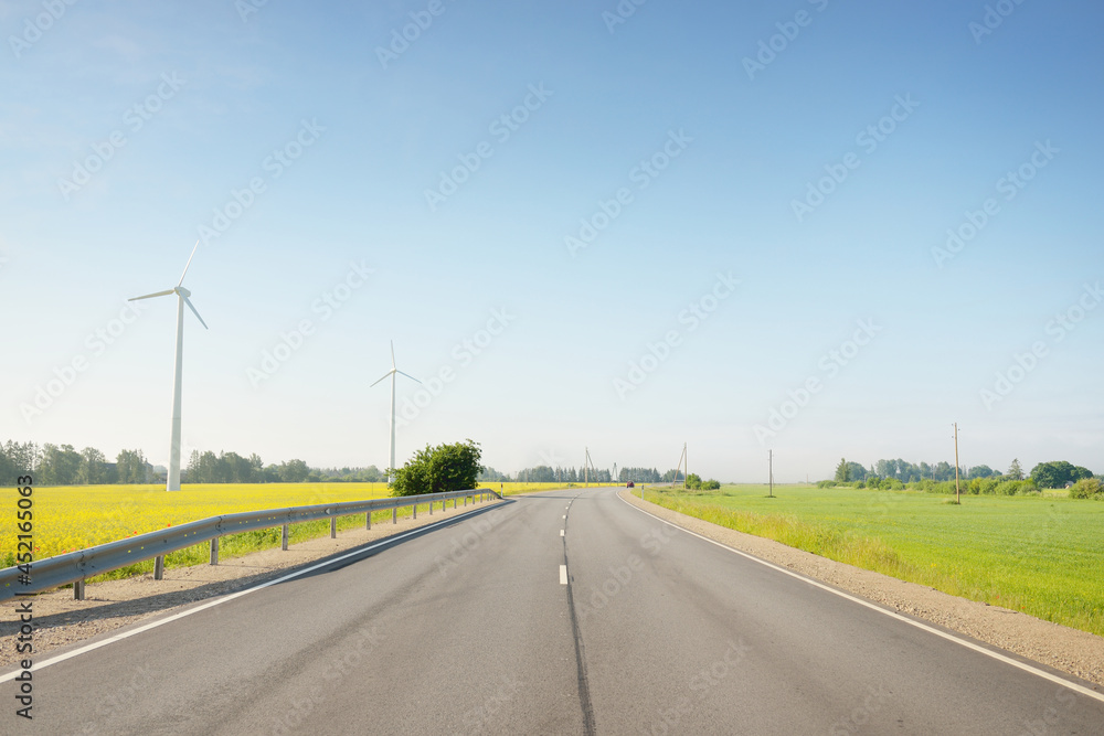 Highway through the blooming rapeseed field and forest at sunrise. Wind ...