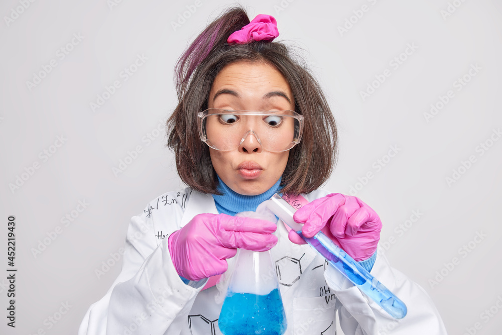 Indoor shot of funny surprised female chemist conducts chemical ...