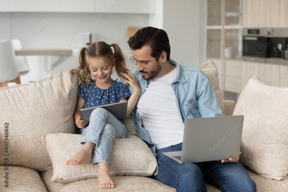 Foto de Happy gen Z little kid and daddy using tablet and laptop ...