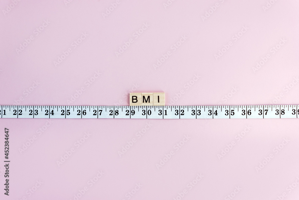 White measuring tape and word BMI on wooden blocks on pastel background ...