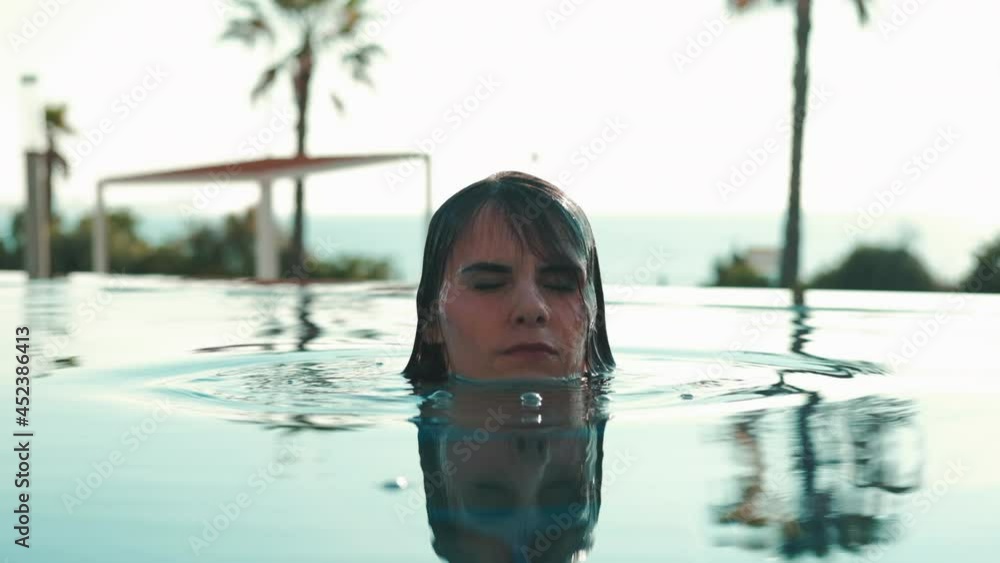 Young 30s brunette woman in swimsuit emerges from the swimming pool ...