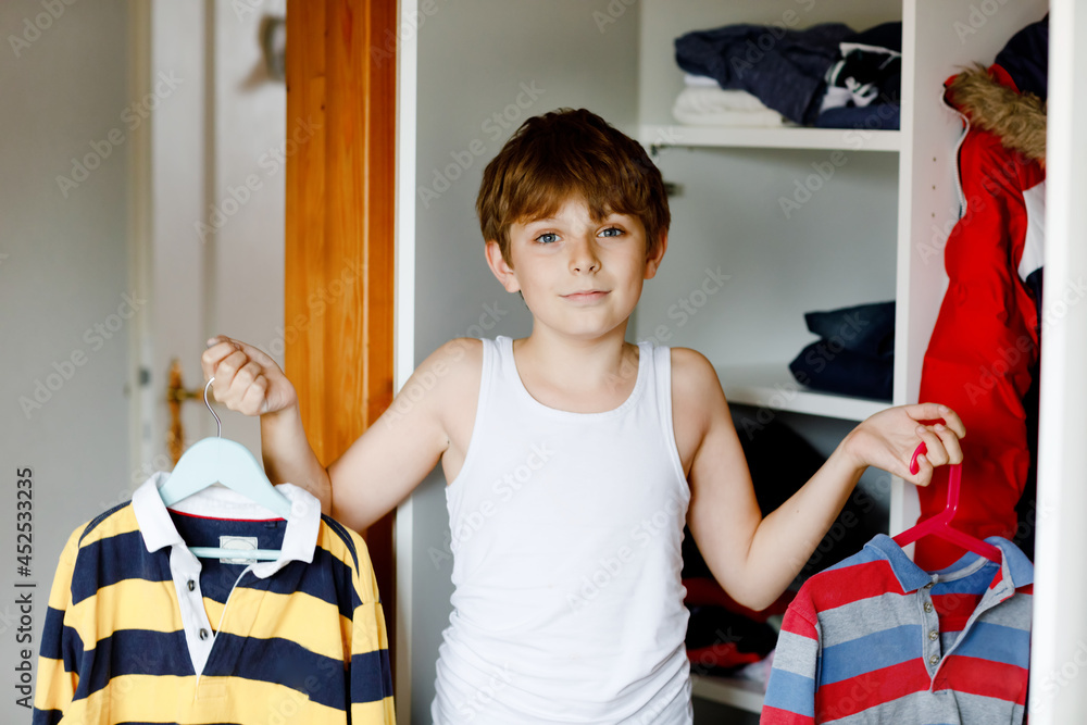 School kid boy standing by wardrobe with clothes. Child making decision ...