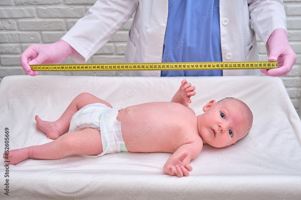 Doctor measures the growth of a newborn baby. A nurse in uniform checks ...
