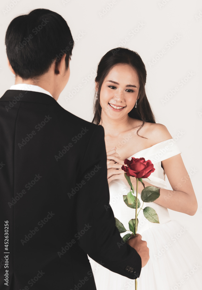 Back of man wearing black tuxedo giving rose to young attractive Asian ...