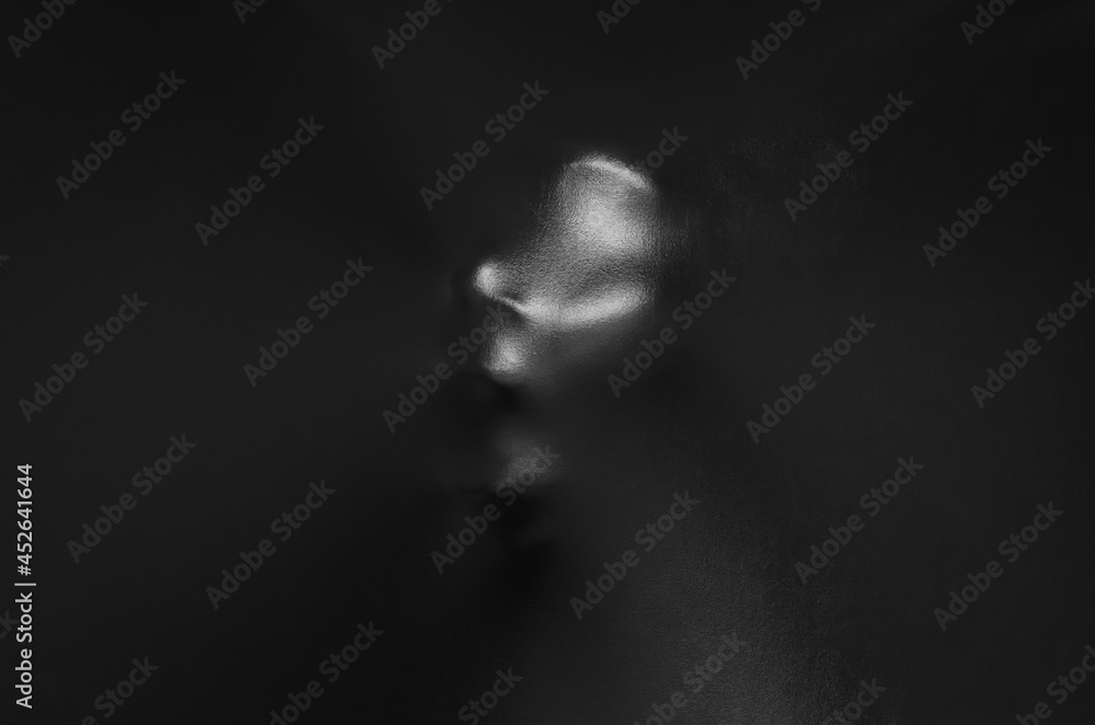 Screaming human face pressing through black fabric with shine and dark ...