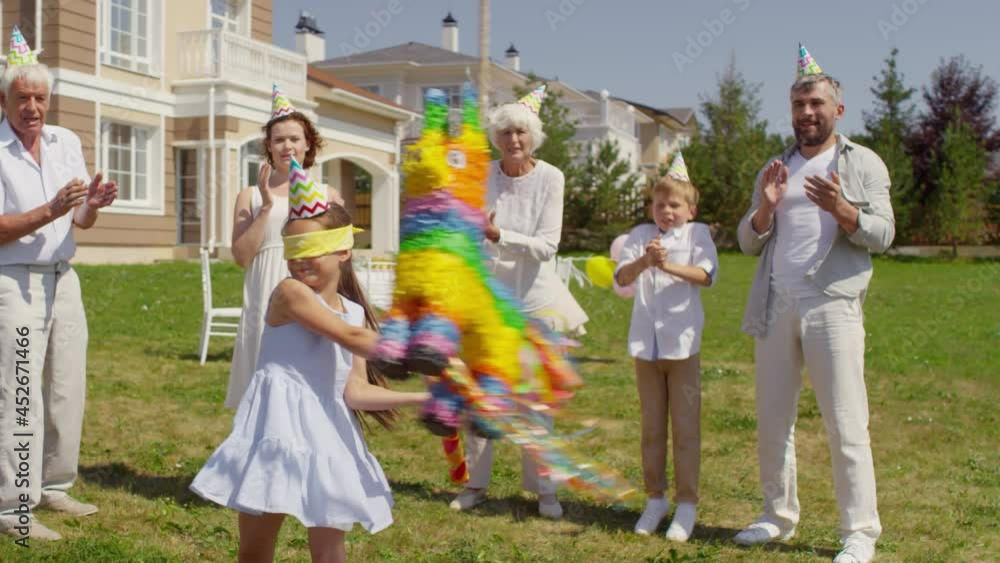 Playful little girl hitting piñata with bat while family members ...