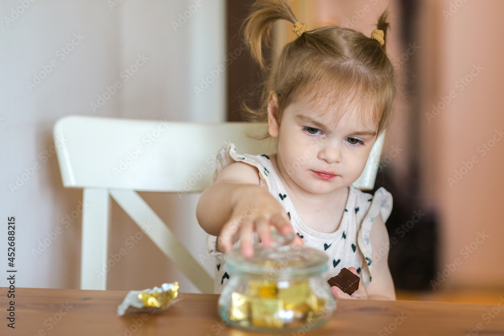 A two-year-old girl reaches for a chocolate candy from a jar. Should ...