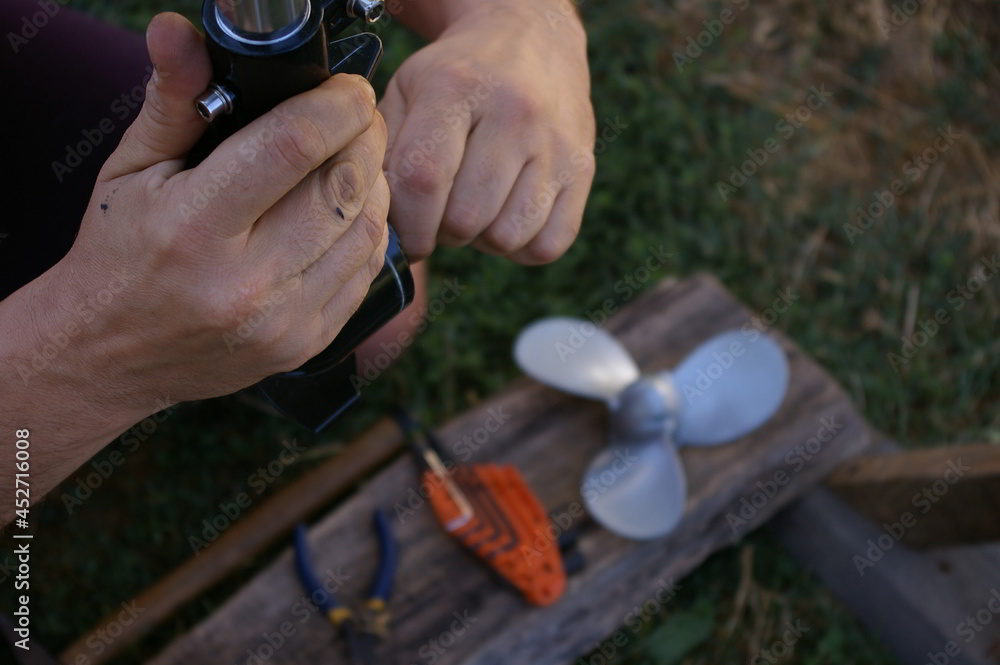 Human hands repairing a propeller boat engine. In the background is the ...