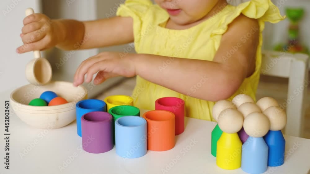 A two-year-old child puts colored balls in a spoon and throws them into ...