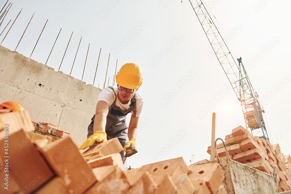 Using bricks. Young construction worker in uniform is busy at the ...
