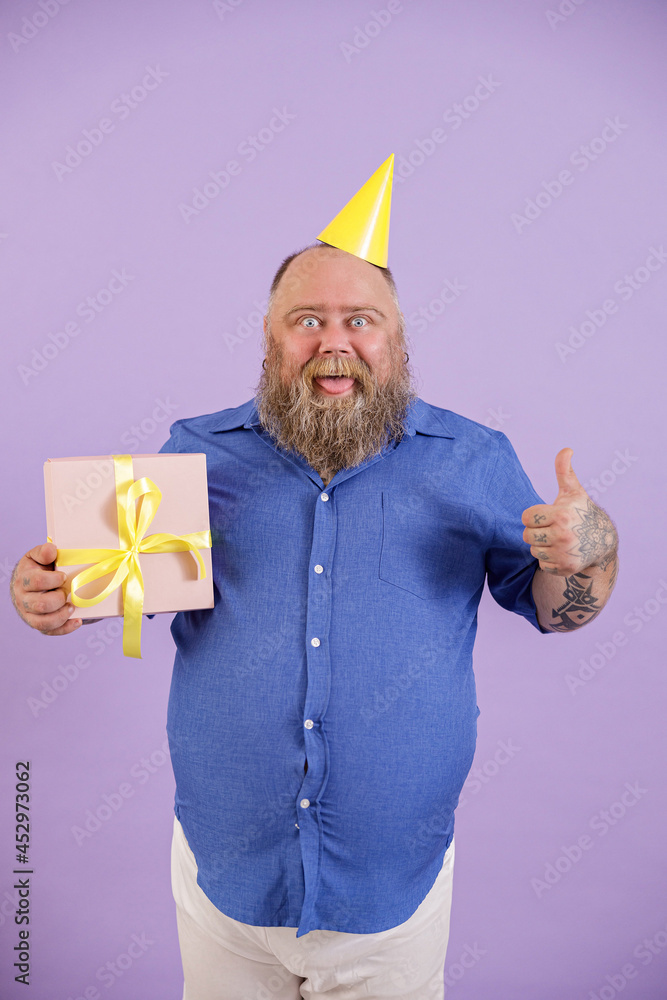 Funny bearded obese man with yellow party hat holds gift box showing ...