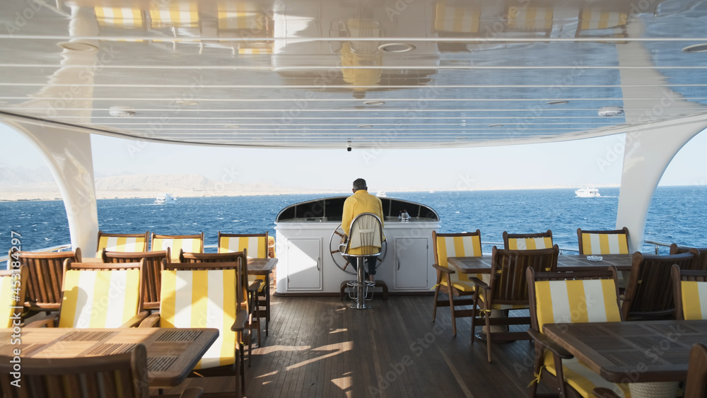 Captain of cruise yacht controls boat, side view. Senior man in yellow ...