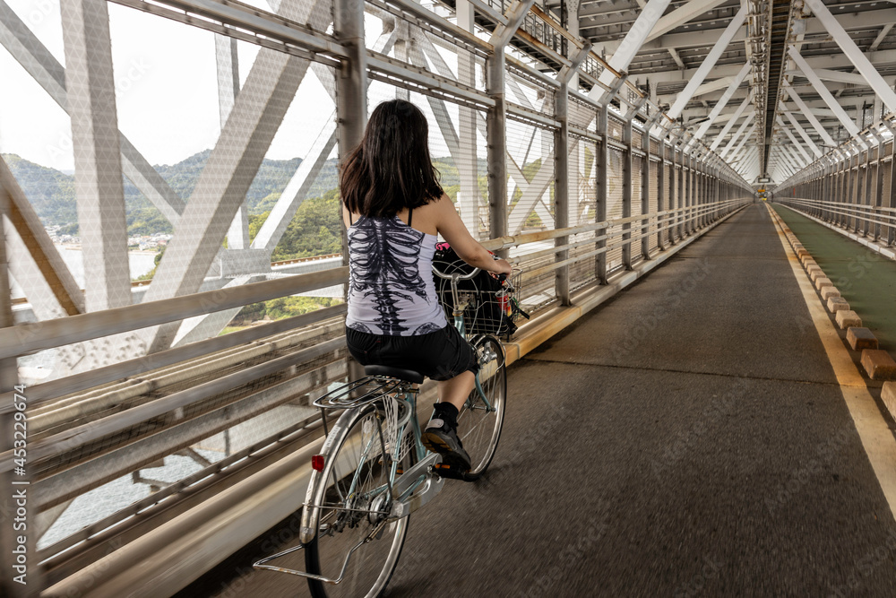 woman riding a bicycle in Japanese cicloway, under the Innoshima Bridge ...