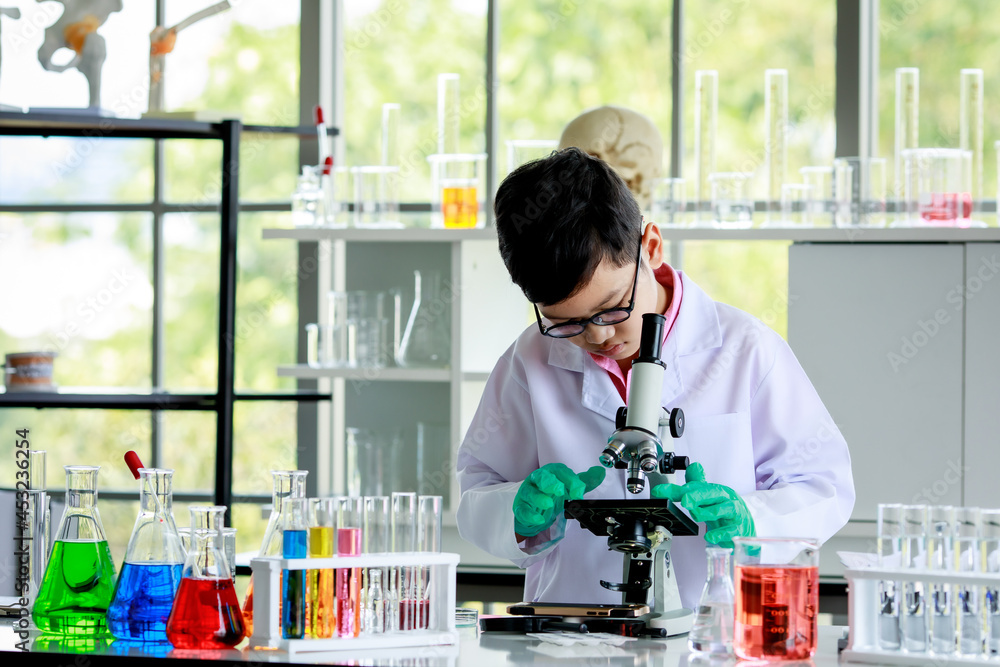 Concentrated smart Asian boy in lab coat and gloves with dropper ...