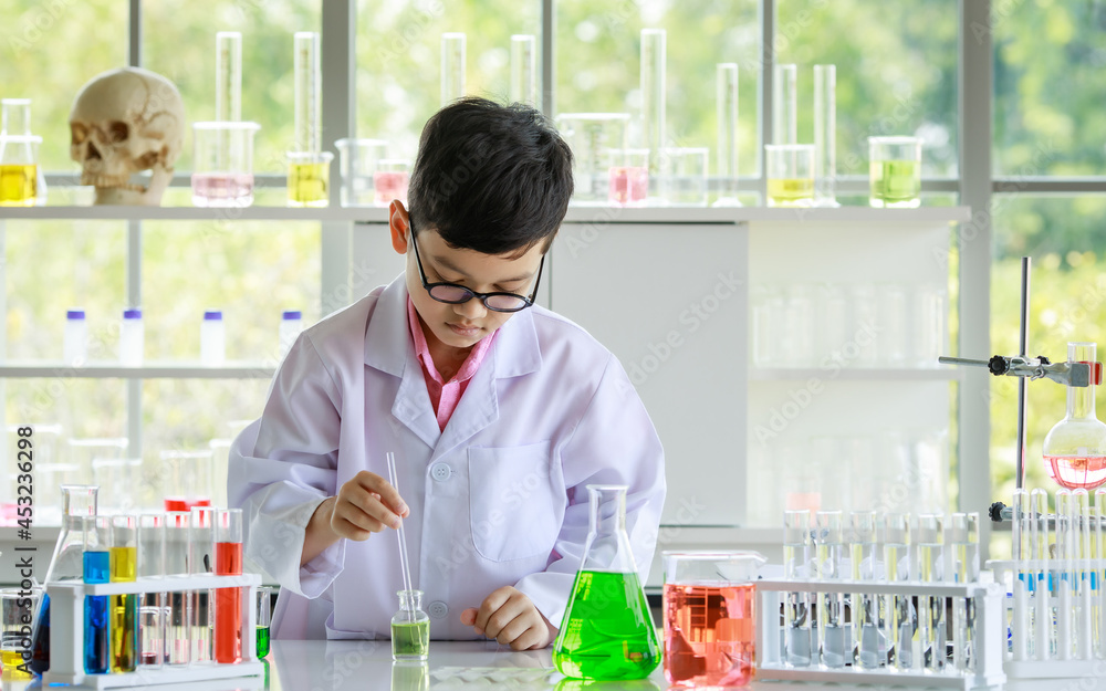 Serious Asian boy in lab coat and glasses with dropper and tube mixing ...