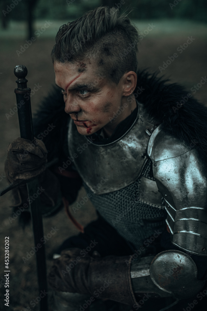 Portrait of medieval knight with bloody face in armour with sword ...