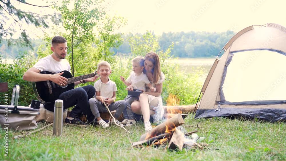 camping by lake in woods. happy family dad mom and little kids sitting ...