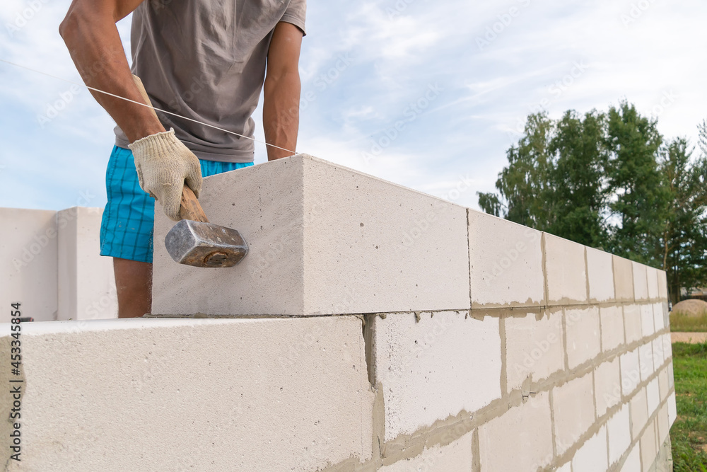 Poster Builder uses a hammer to tamp aerated concrete blocks on the ...