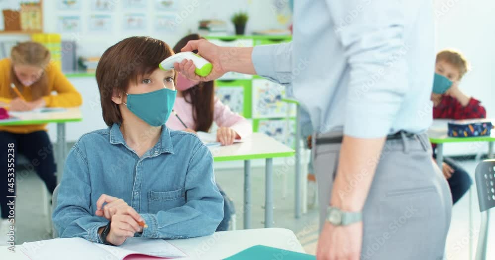 Female teacher's hand in classroom measuring temperature of Caucasian ...