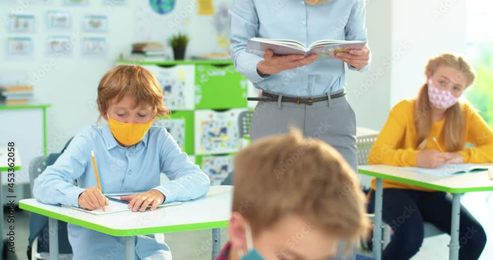 Female teacher explains reading lesson to a diverse classroom of bright ...