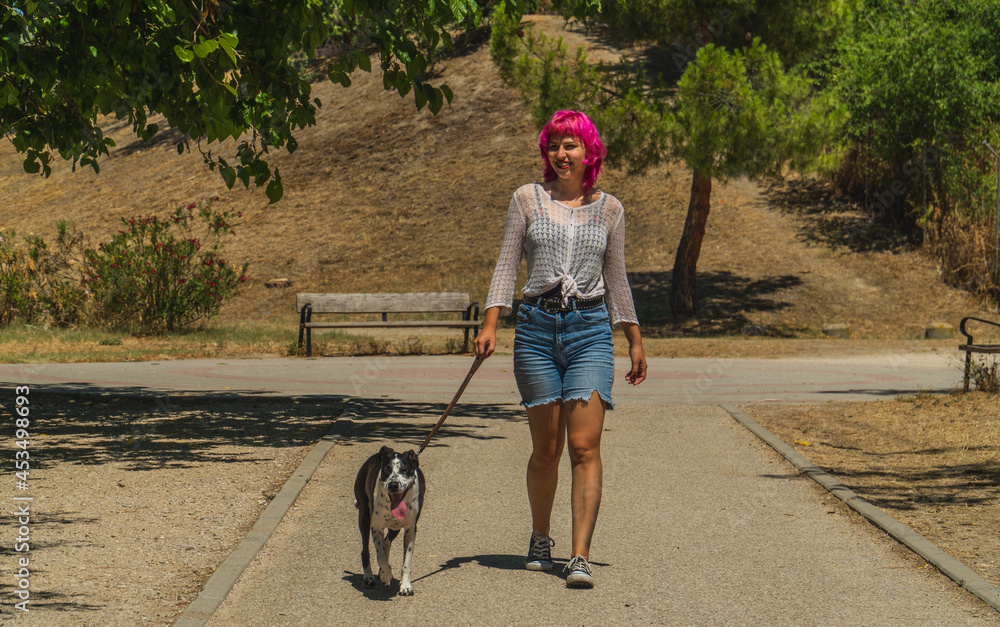 Joven mujer de pelo rosa paseando a un perro blanco y negro en el ...
