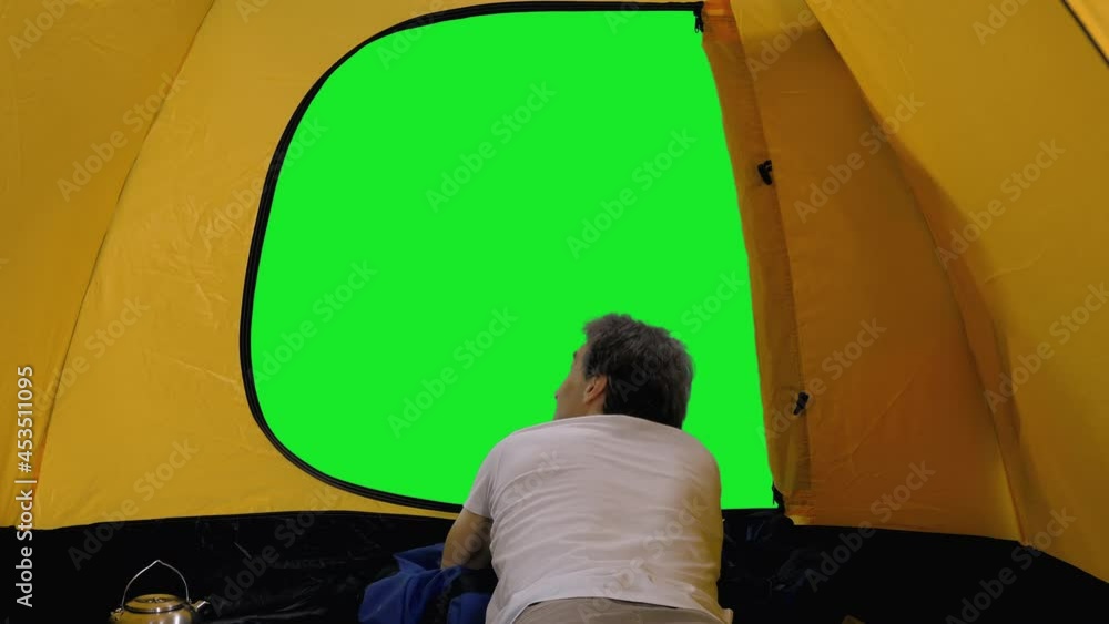 Rear view of man hiker lying inside tent and looking out on green ...