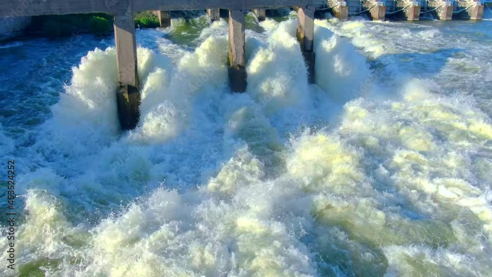 Water flowing fast between some concrete pillars. Though the pillars ...