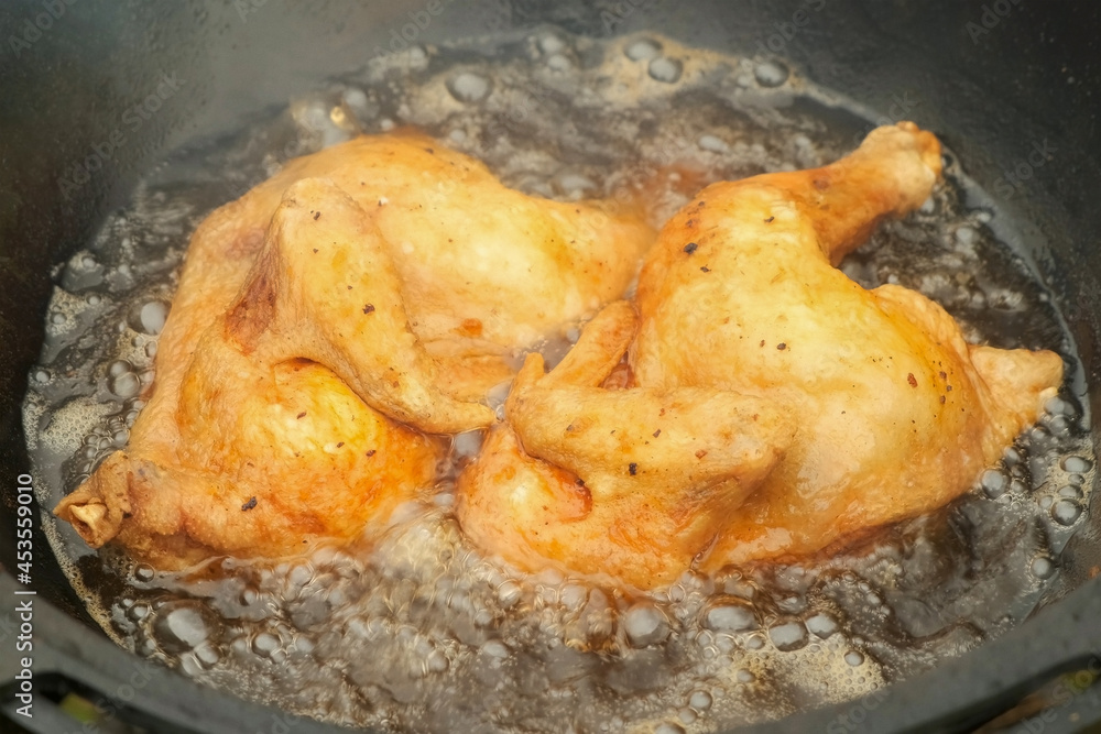 Frying chicken in black cazan with boiling oil in wood-burning stove on ...