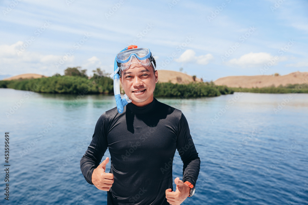 Smiling Asian man in snorkeling mask wearing wetsuit giving thumb up on ...