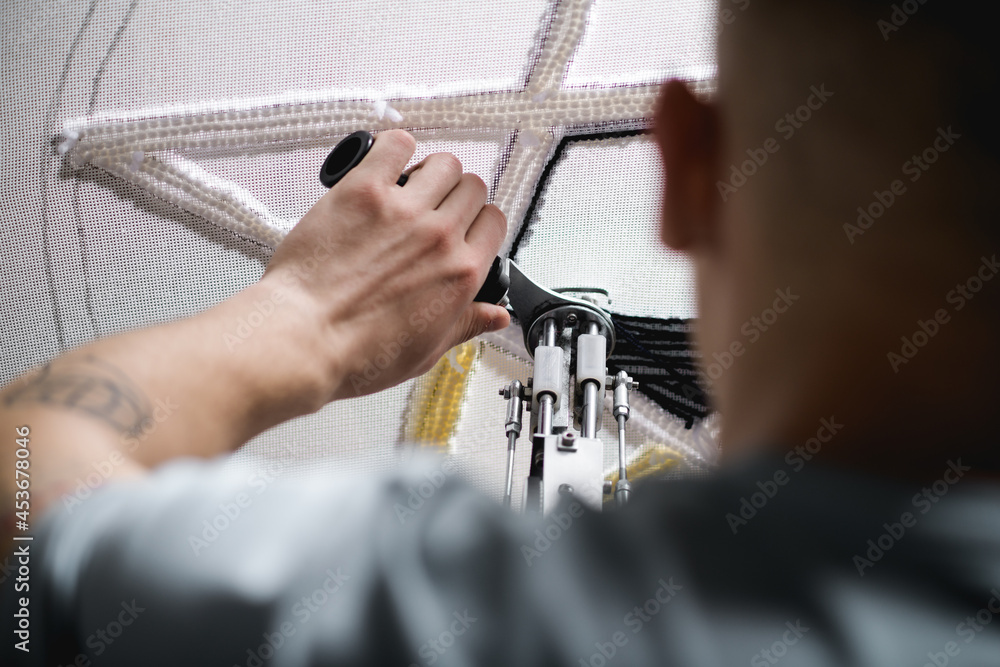 Back view of rug maker with tufting machine creating pattern on canvas ...