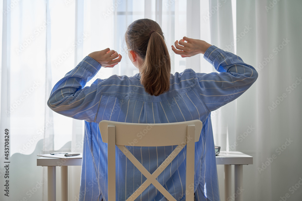 Back view of young female sitting at desk and stretching. Remote work ...
