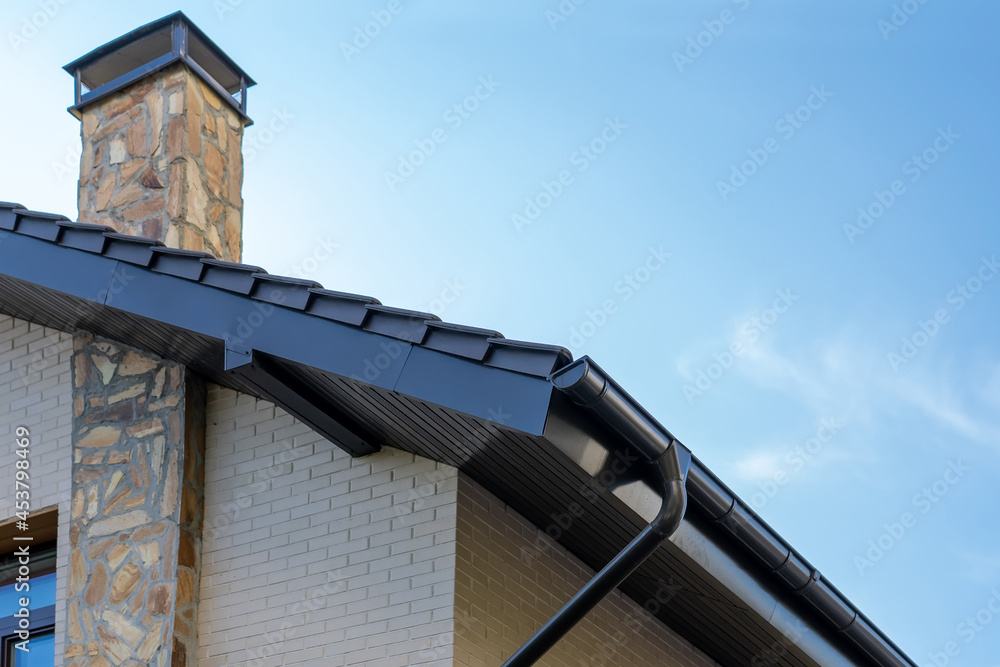 Brick house with drainage system on metal roof. Сhimney pipe is ...
