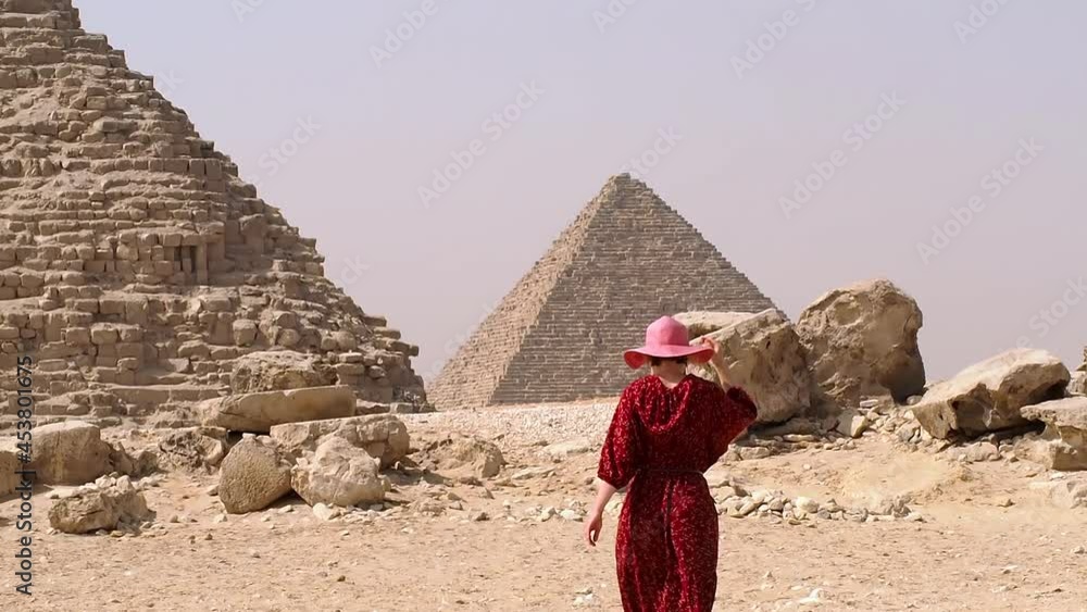 A tourist in a red dress and hat walks by the pyramids of Giza on a ...