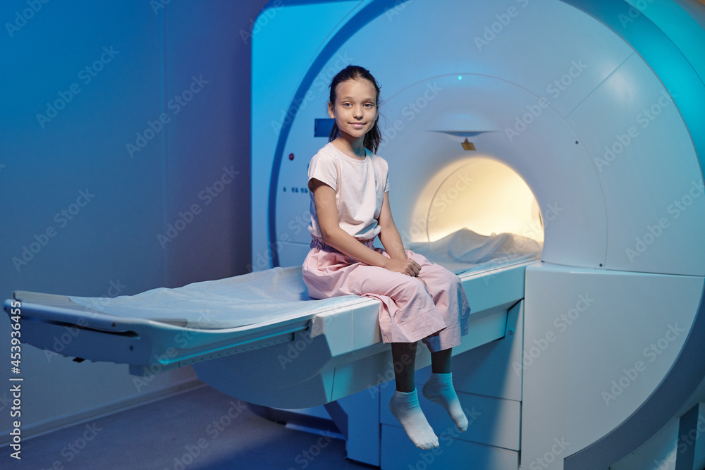 Smiling little patient sitting on long medical table before or after ...