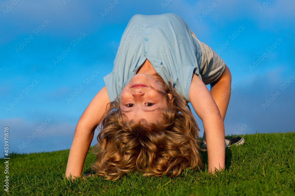 Happy boy doing a headstand on the grass in the summer sunshine. Funny ...