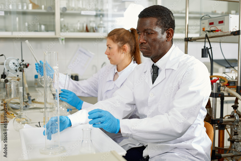 Focused lab technicians in gloves working with glass test tubes before ...